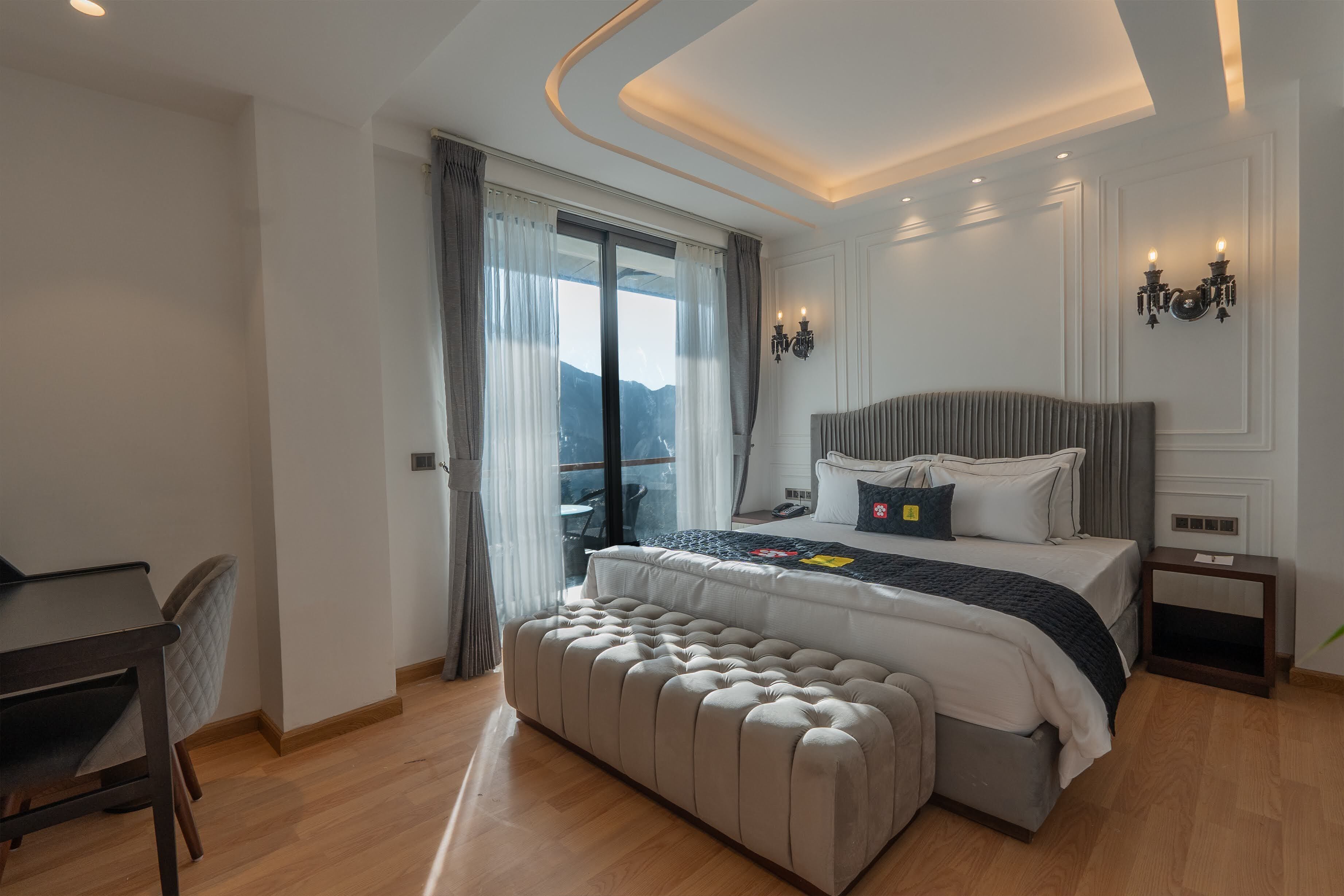Quarto moderno com uma cama grande, uma escrivaninha e vista para montanhas pela janela.