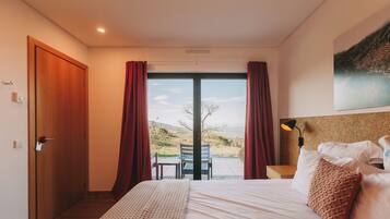 Quarto de hotel com uma cama grande, uma escrivaninha, uma cadeira e vista para o campo.