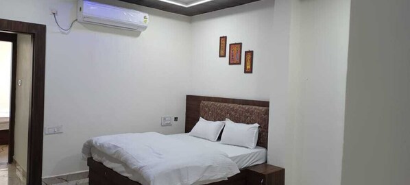 Quarto com cama, mesas de cabeceira, ar condicionado fixado na parede e três quadros na parede.