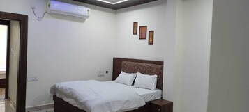 Quarto com cama, mesas de cabeceira, ar condicionado fixado na parede e três quadros na parede.