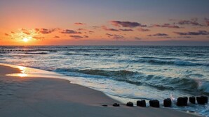 Uma praia com um píer de madeira que se estende para o oceano durante o pôr do sol.