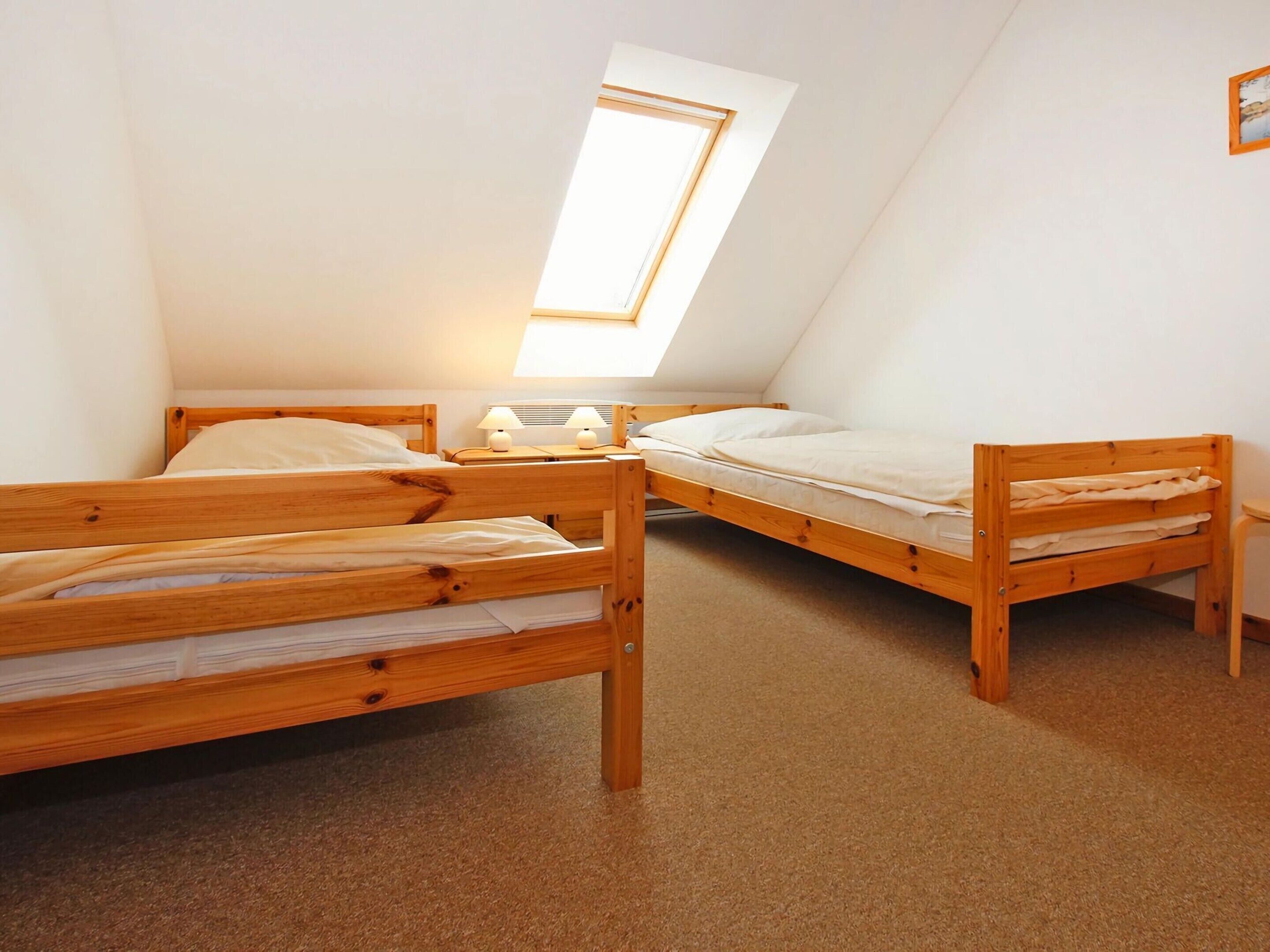 Um quarto de sótão pequeno e triangular com duas camas beliche de madeira, um claraboia e uma pequena mesa de cabeceira com abajures.