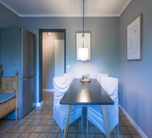 Uma área de refeições com mesa e cadeiras, um lustre pendurado e uma porta que dá para outro cômodo.
