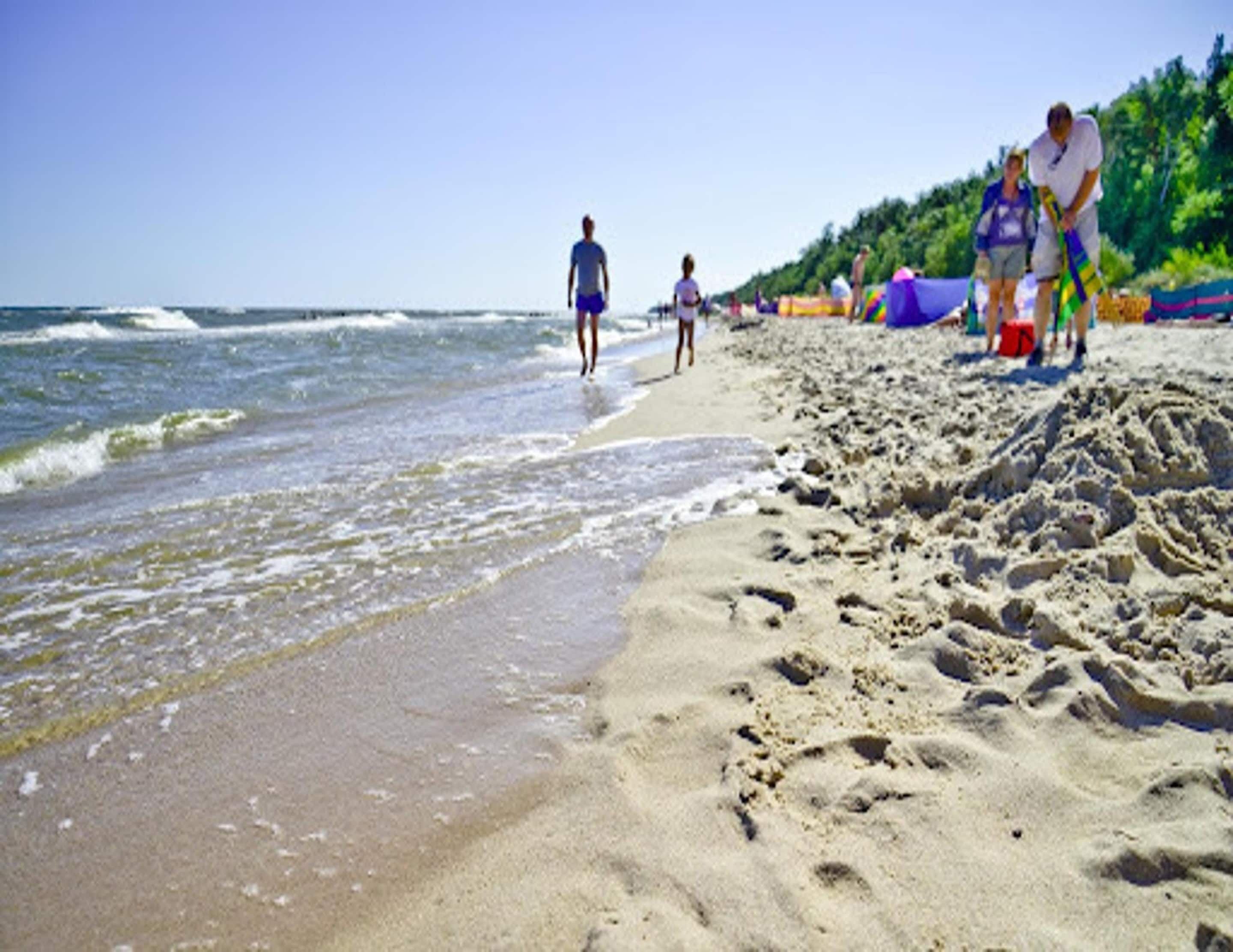 Uma praia arenosa com pegadas, céu claro e pessoas caminhando pela orla.
