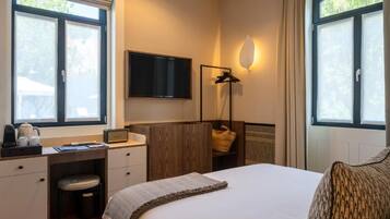 Quarto de hotel com cama, escrivaninha, cadeira, televisão e janela com cortinas.