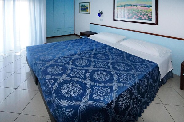 Quarto com cama, mesa de cabeceira, guarda-roupa e duas imagens emolduradas na parede.