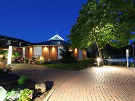 Um edifício com telhado em forma de cúpula, entrada com calçada e jardim bem cuidado.