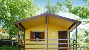 Um edifício amarelo com base de pedra, varanda de madeira e uma pequena janela com persianas.
