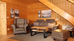 Interior acolhedor de uma cabana de madeira com escada de madeira, sofás de couro, uma mesa pequena e uma lareira.