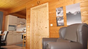 Interior acolhedor de cabana, com decoração em madeira, área de jantar e espaço de estar com uma poltrona de couro.