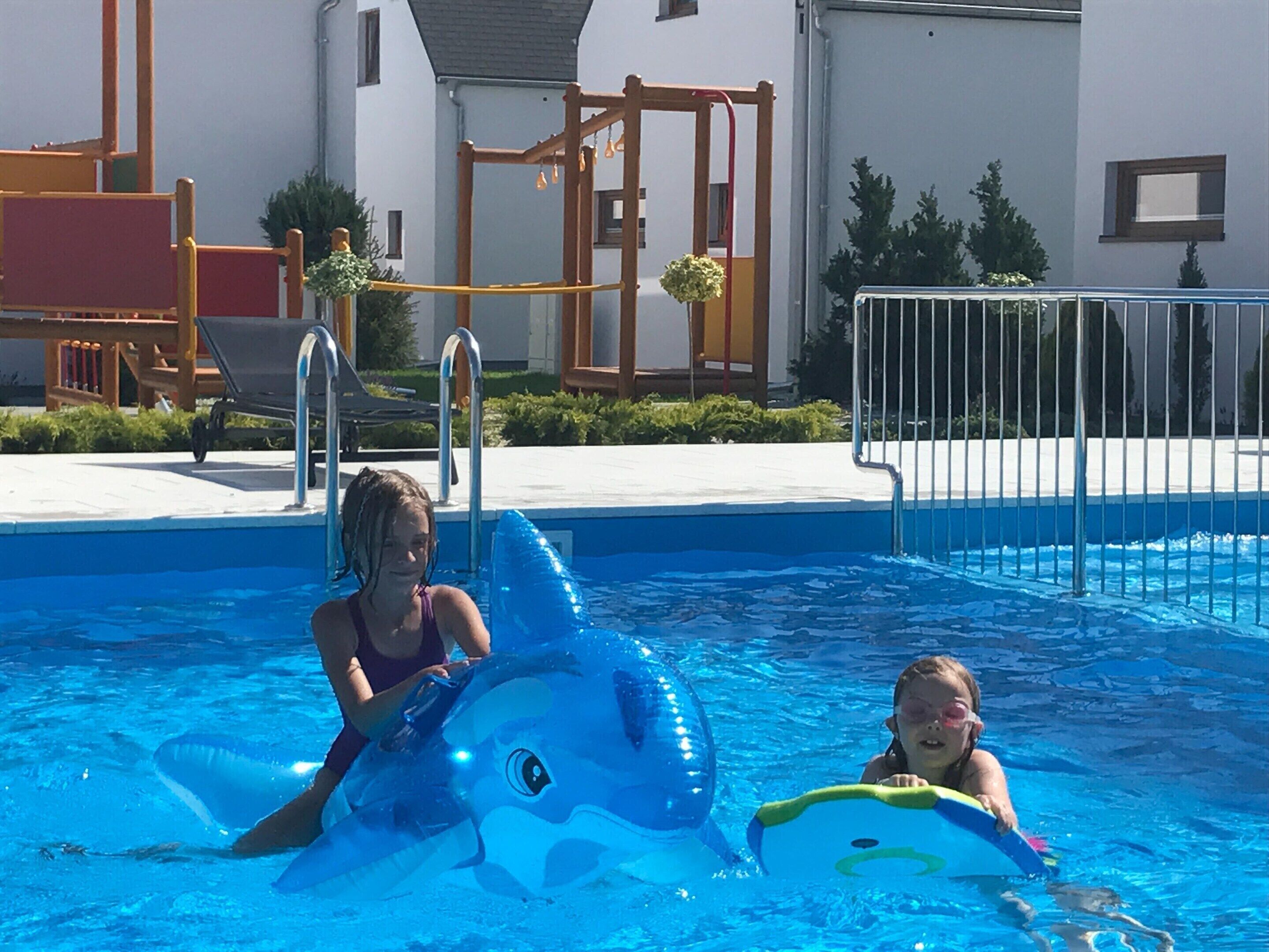 Piscina com área de recreação infantil, incluindo um escorrega e uma estrutura de escalada.