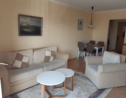 Uma sala de estar com um sofá, duas mesas redondas, uma mesa de jantar com cadeiras e um quadro na parede.