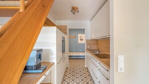 Cozinha estreita com piso estampado, armários de madeira e uma máquina de café embutida.