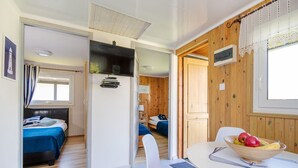 Quarto moderno com cama, escrivaninha e mesa de jantar. Há uma janela com cortinas e vista para o exterior.