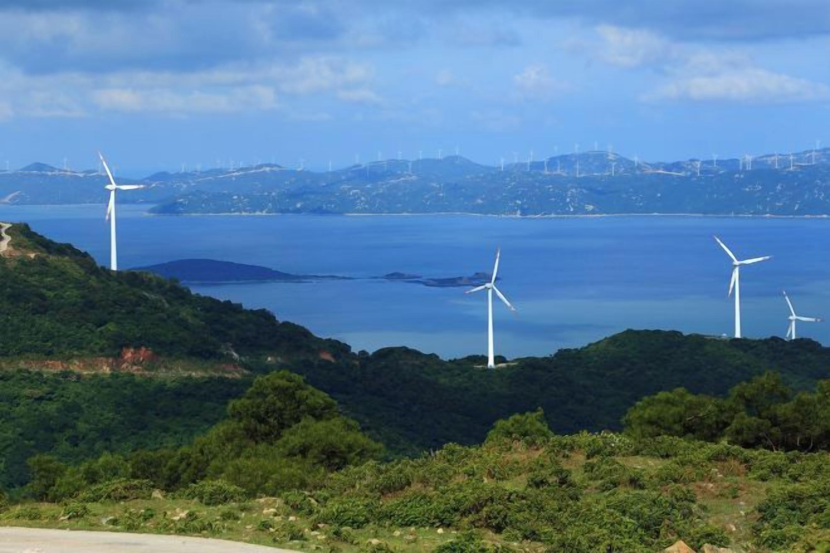 Paisagem costeira com turbinas eólicas e relevo acidentado.