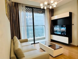 Uma sala de estar moderna com um sofá, uma mesa de centro, uma televisão de tela plana na parede e uma janela grande com cortinas.