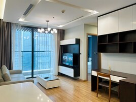 Uma sala de estar moderna com um sofá, uma mesa de centro de vidro, uma televisão e uma área de jantar com mesa e cadeiras.