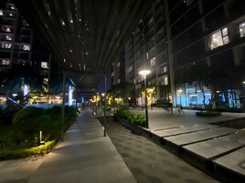 Vista noturna de um edifício moderno com galeria coberta, área de estar ao ar livre e janelas iluminadas.