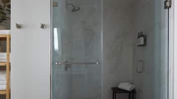 Um chuveiro com divisória de vidro, um corrimão, uma pequena mesa com uma toalha e um chão ladrilhado com padrão geométrico.