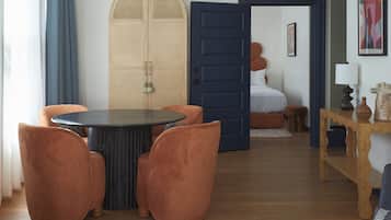 Uma sala de estar moderna com uma mesa redonda, duas cadeiras laranja, uma porta azul e piso de madeira.