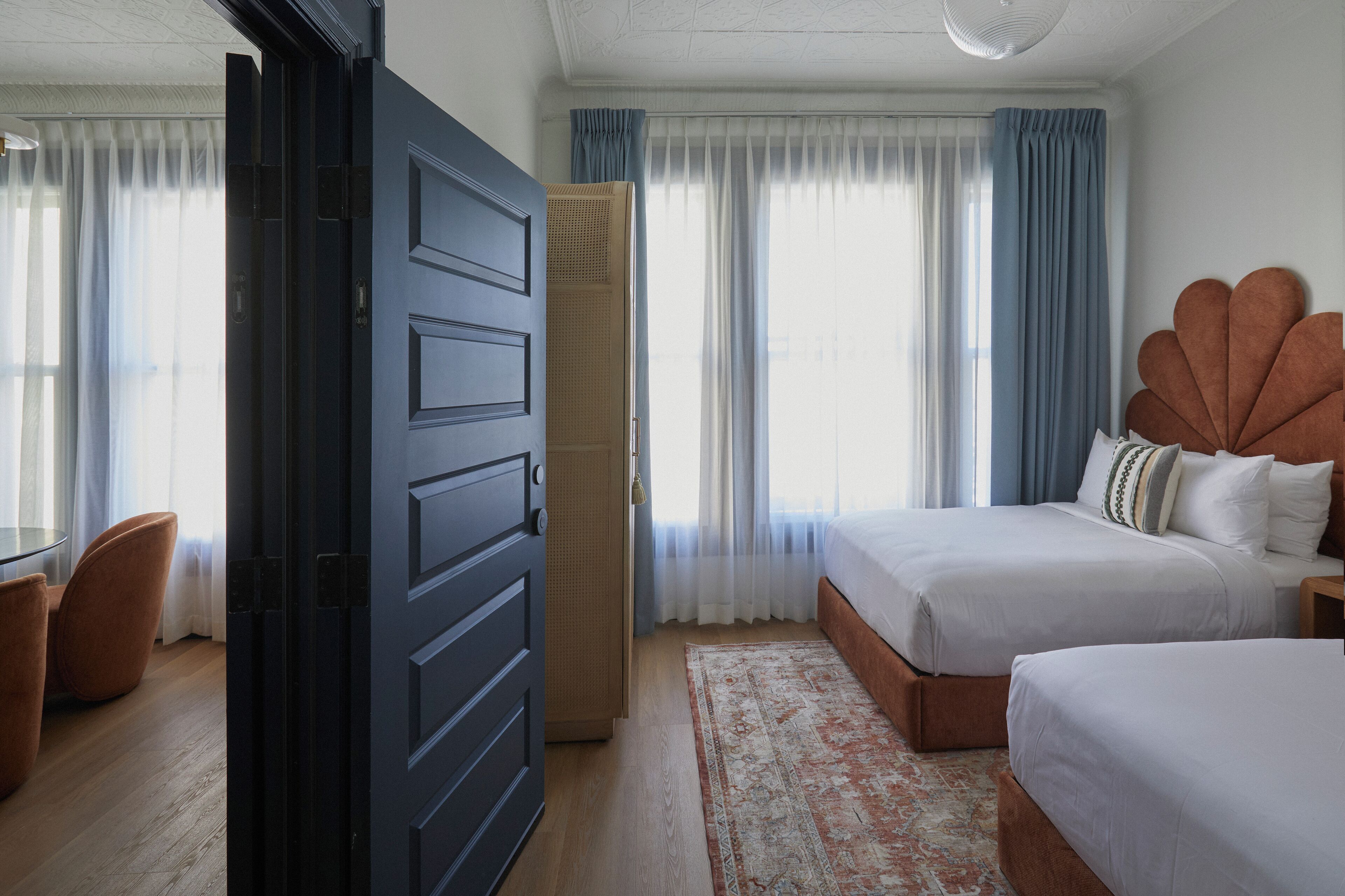 Quarto de hotel com uma cama grande, uma cama menor, uma escrivaninha com cadeiras e um guarda-roupa.