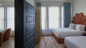 Quarto de hotel com uma cama grande, uma cama menor, uma escrivaninha com cadeiras e um guarda-roupa.