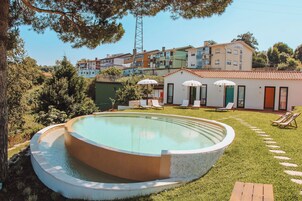 Piscina com deck ao redor, cadeiras de descanso e guarda-sóis.