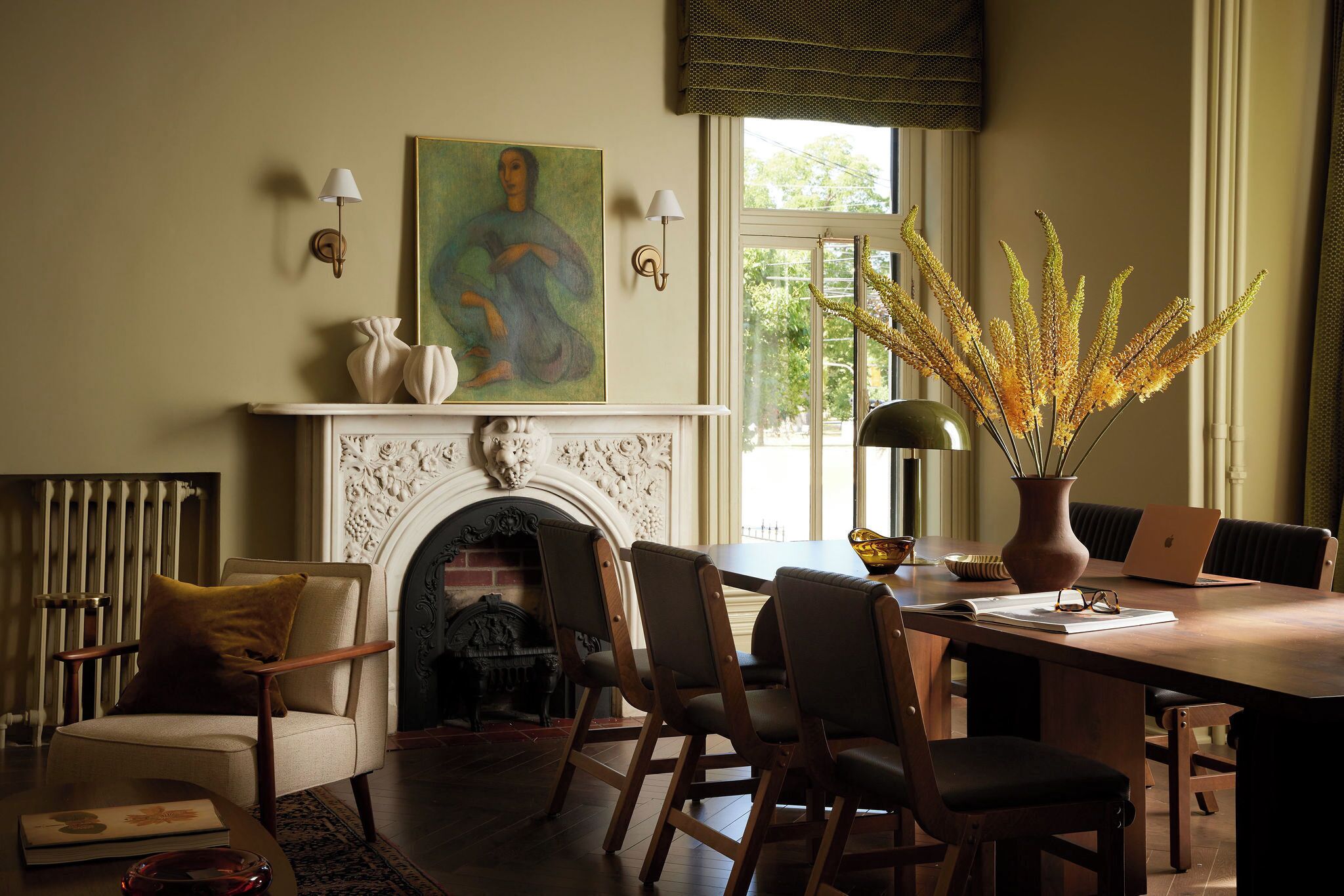 Uma sala de jantar com lareira, um quadro e um vaso com plantas secas.
