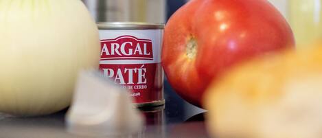 Uma bancada de cozinha com uma lata de Argal Paté, um tomate vermelho, uma cebola branca e um pepino amarelo.