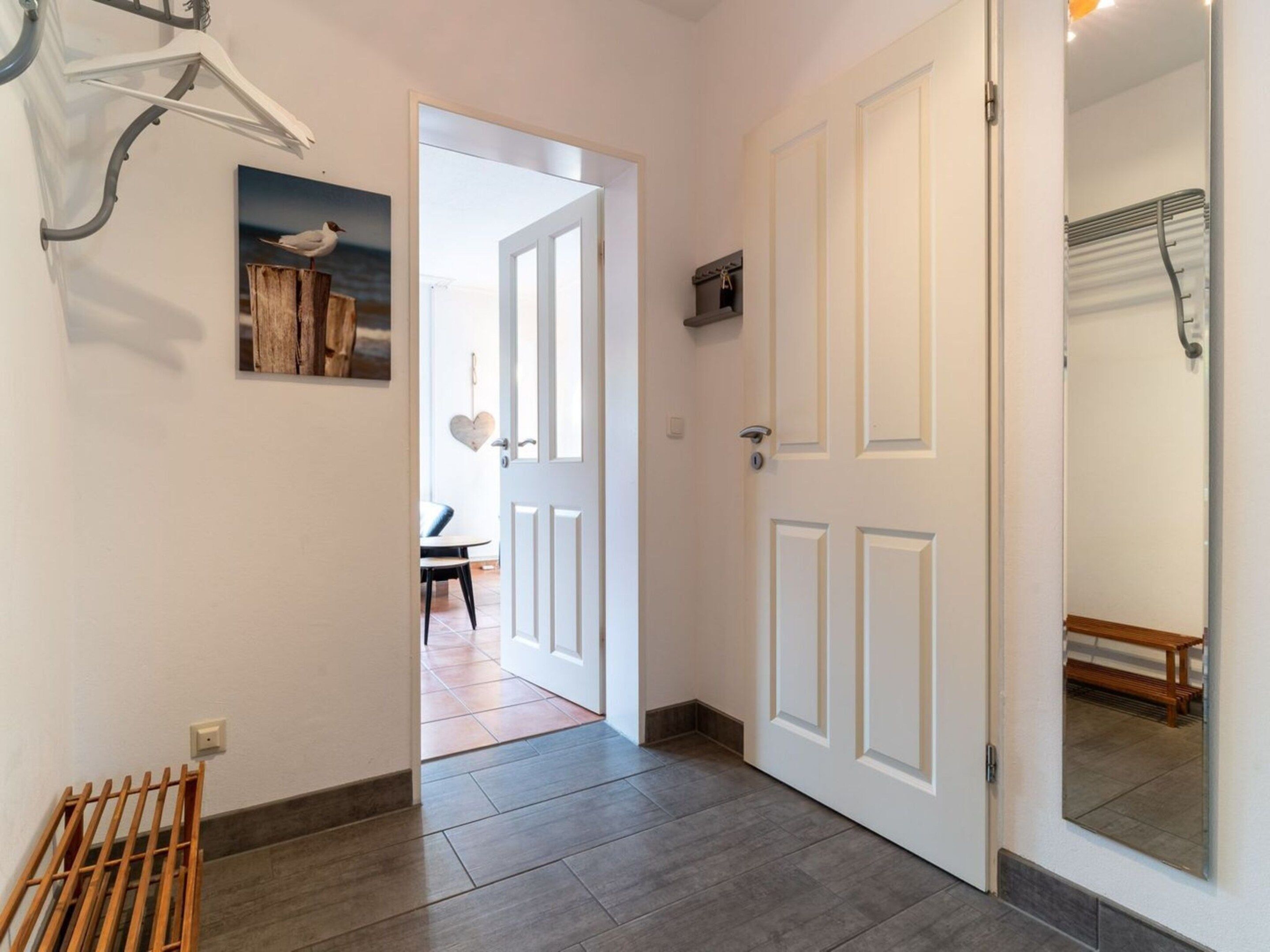 Um corredor com um banco de madeira, um cabide e uma porta que dá para outro quarto.