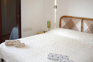 Quarto com cama, mesa de cabeceira, abajur e porta.