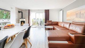 Uma sala de estar moderna com um sofá de couro marrom, uma mesa de jantar com cadeiras, uma lareira e uma janela grande com cortinas.