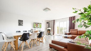 Uma sala de estar moderna com sofá, área de jantar com mesa e cadeiras, lareira e uma janela grande com cortinas.