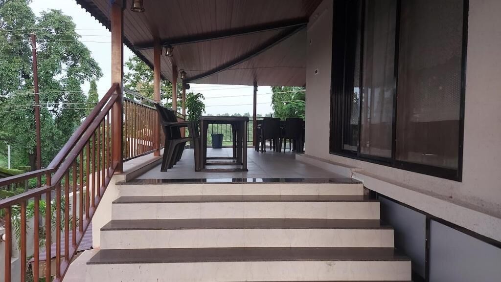 Uma área externa coberta com degraus que levam a uma mesa e cadeiras, cercada por grades e árvores.