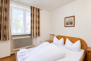 Quarto de hotel com cama, cadeira, radiador, janela com cortinas e um quadro na parede.