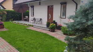Uma casa com telhado telhado, varanda frontal com duas cadeiras, uma mesa de jantar e um guarda-sol grande.