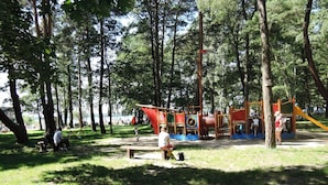 Um parque com parquinho, mesas para piquenique e um lago ao fundo.