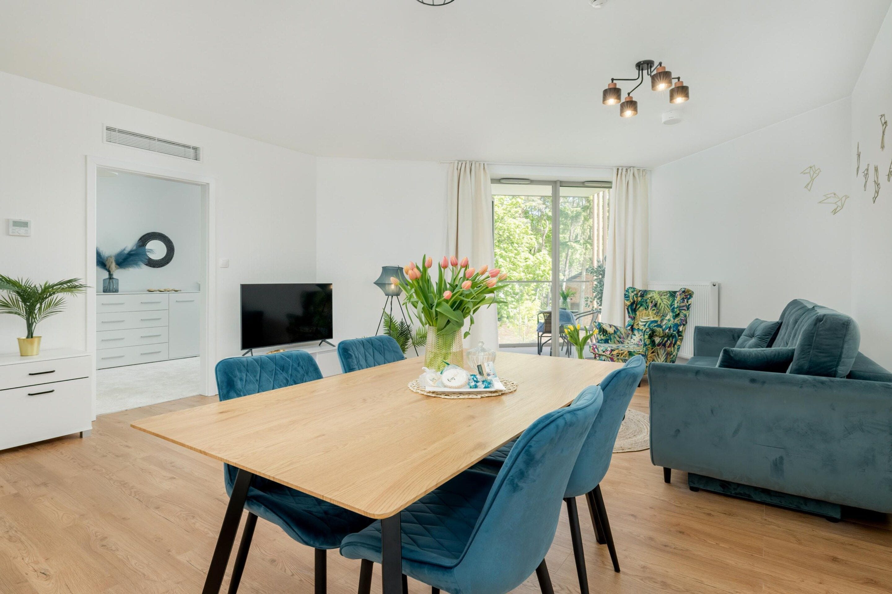 Uma sala de estar moderna com uma mesa de jantar de madeira, cadeiras estofadas em azul, um sofá azul e uma televisão.