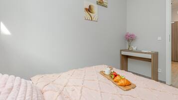 Quarto com cama, mesa de cabeceira com um vaso e flores, e bandeja com comida e um croissant.