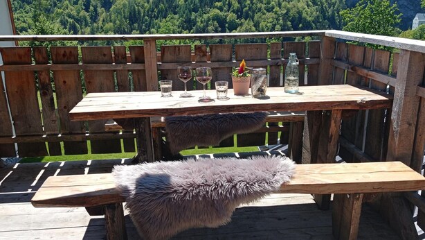 Um deck de madeira com mesa e bancos, cercado por uma cerca de madeira, com vista para uma encosta arborizada.