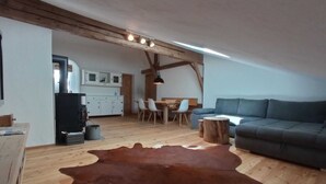 Uma sala de estar aconchegante com sofá, mesa de jantar e cadeiras, cozinha com armários e piso de madeira.
