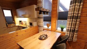 Interior de madeira com mesa de jantar, cadeiras, área de cozinha e janela com cortinas.