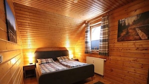 Quarto de cabana aconchegante com uma cama, duas mesas de cabeceira, uma janela com cortinas e um quadro na parede.