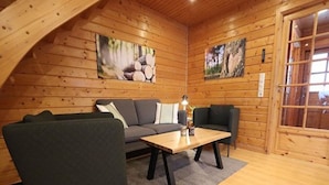 Interior acolhedor de uma cabana de madeira, com um sofá, duas poltronas, uma mesa de centro e paredes de madeira.