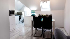 Uma cozinha moderna com armários brancos, micro-ondas e um espaço de refeições com duas cadeiras pretas e uma mesa.