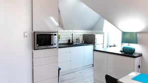 Cozinha moderna com armários brancos, bancada preta, micro-ondas, geladeira e luminária verde-água.