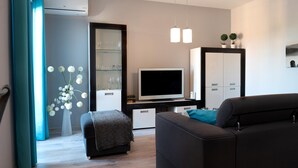 Uma sala de estar moderna com televisão de tela plana, sofá, mesa de centro e um vaso decorativo com flores brancas.