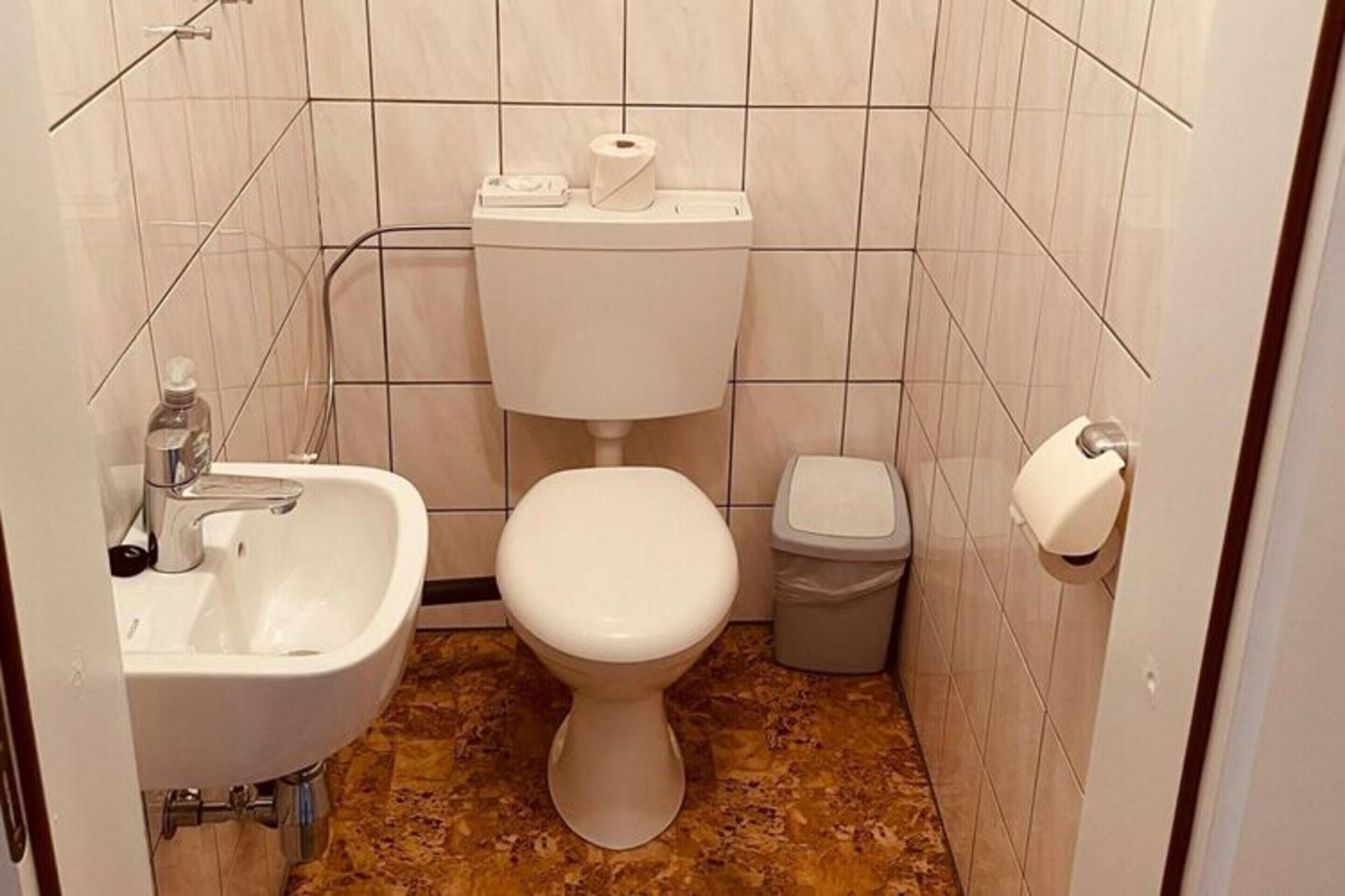 Casa de banho pequena com sanita, lavatório e caixote de lixo.
