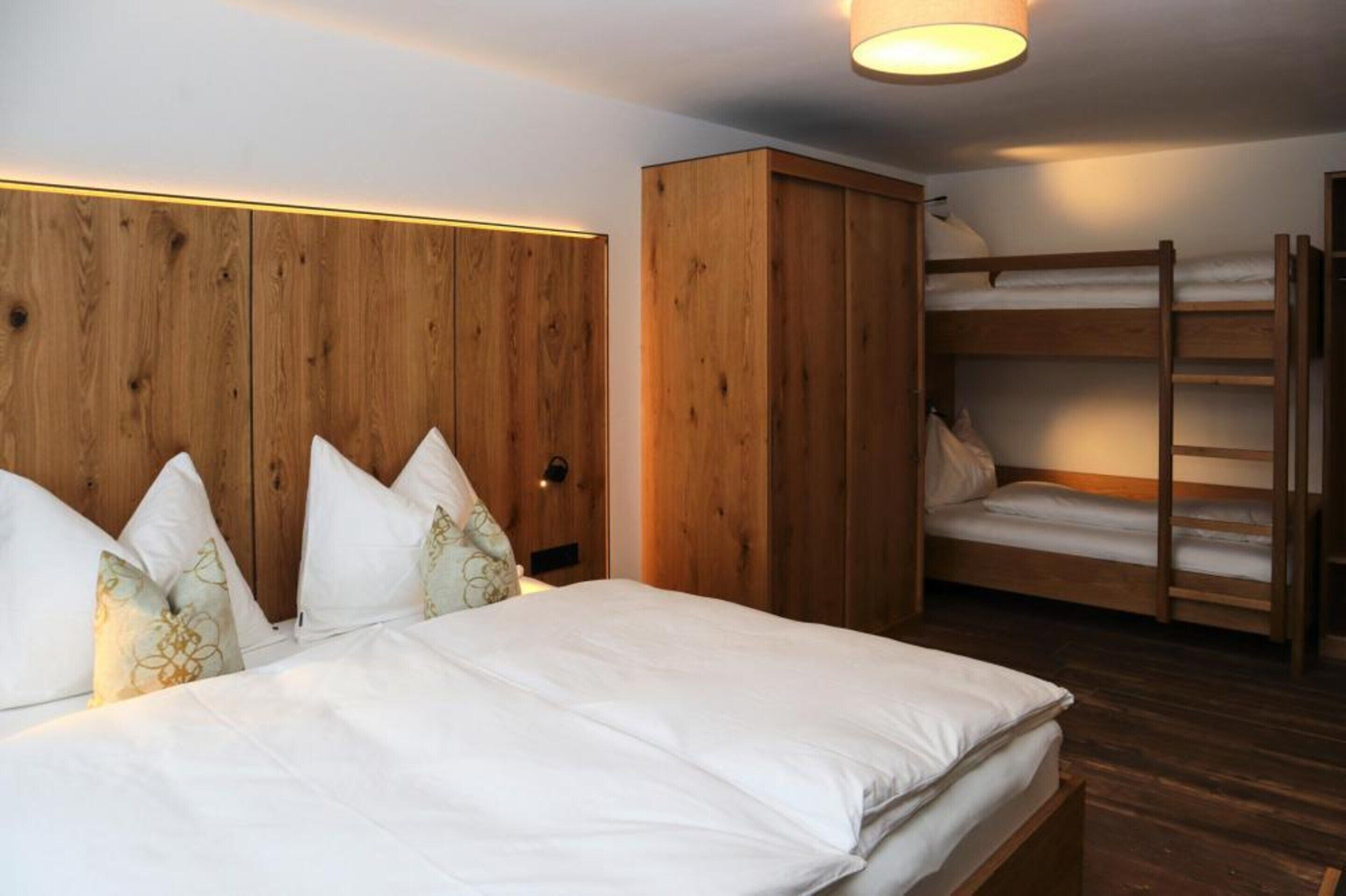 Quarto com cama beliche de madeira, guarda-roupa grande e cama com roupa de cama branca.