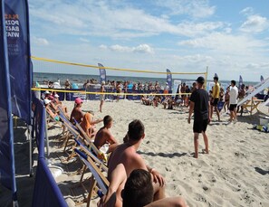 Jogo de voleibol de praia com jogadores e espectadores na areia.